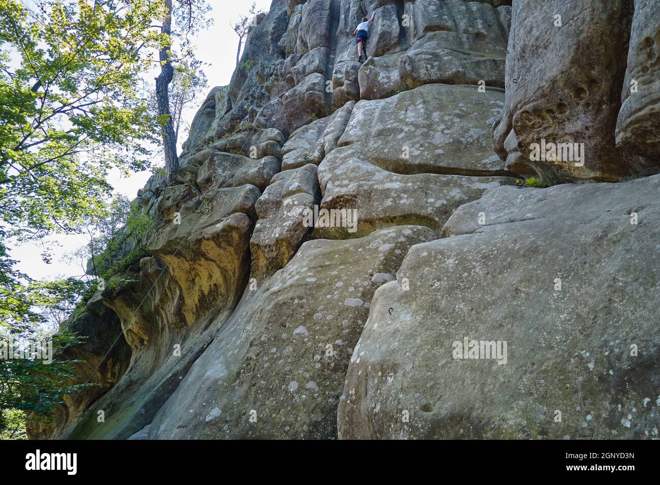 Determined boy climber clambering up steep wall of rocky mountain ...