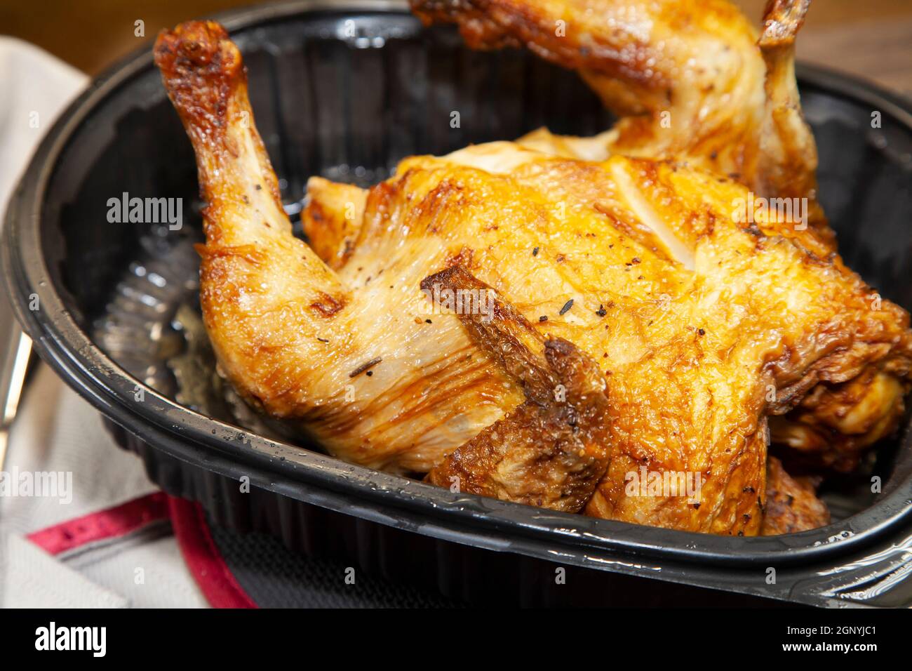 Whole roasted chicken in a black carryout container next to a grey ...