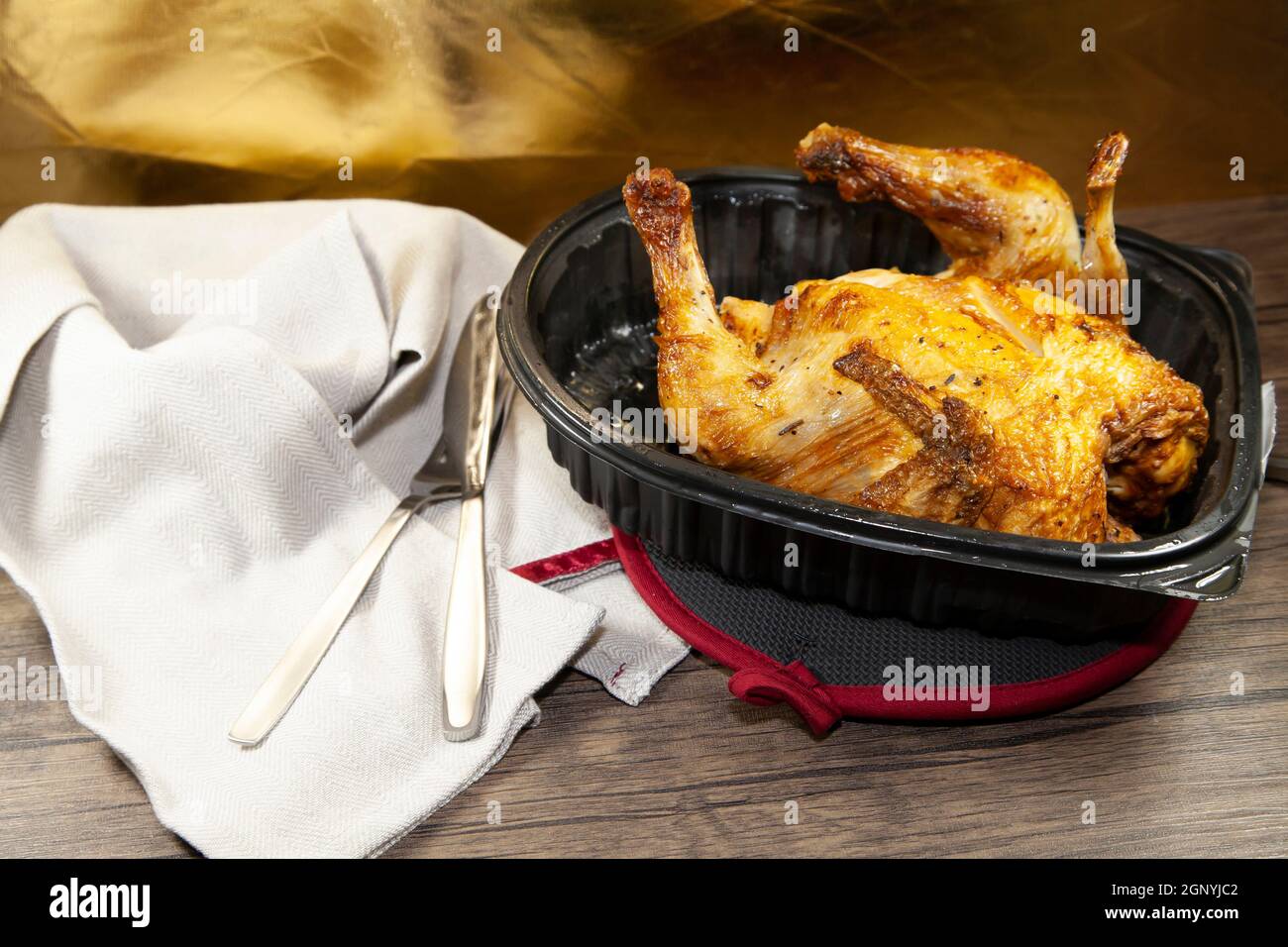 Whole roasted chicken in a black carryout container next to a grey ...