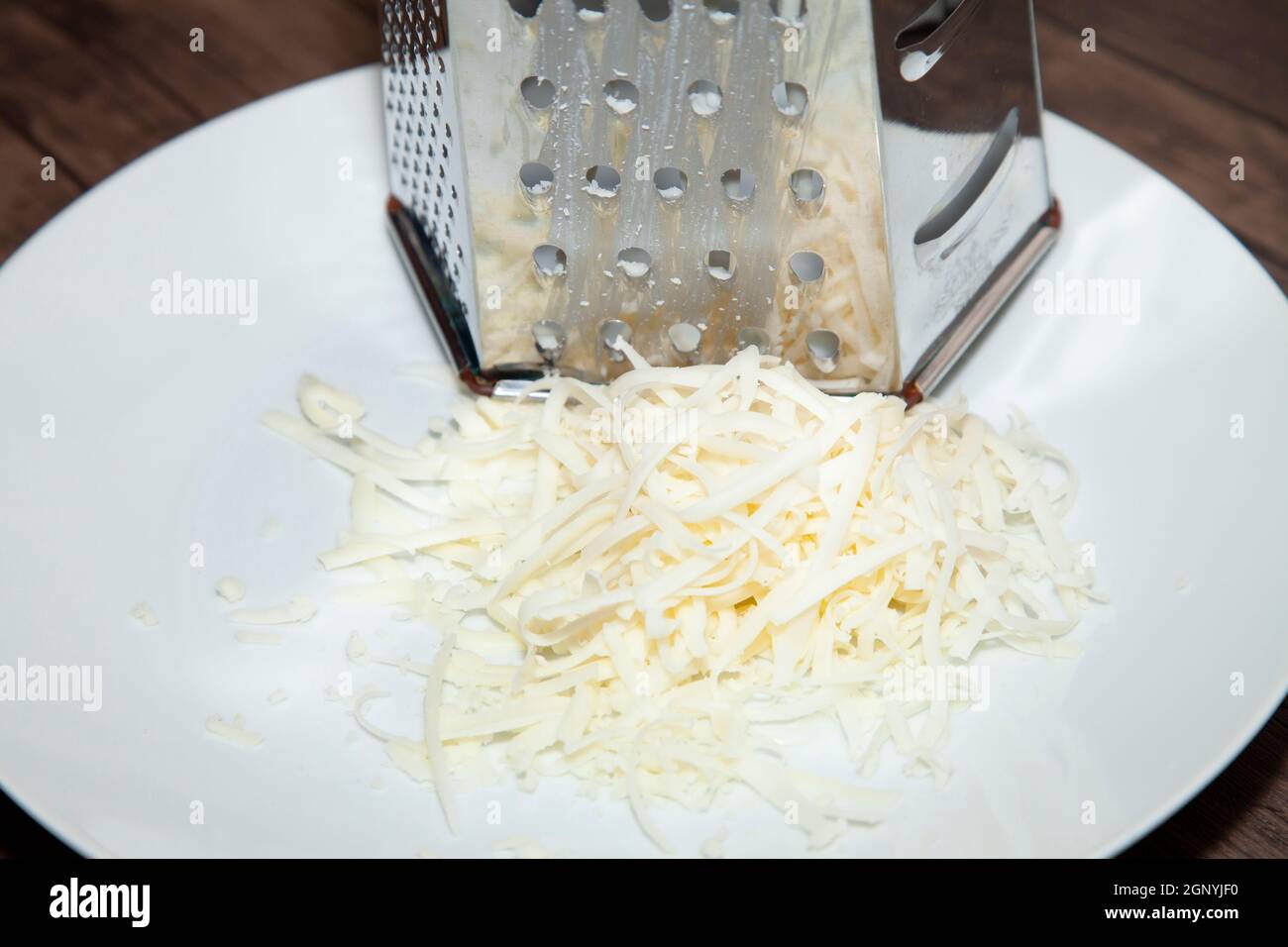 Pile of shredded white cheese on a white plate next to a large, metal ...