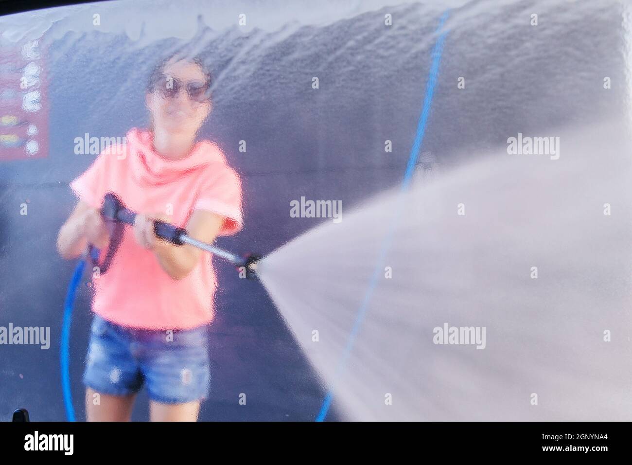 Woman washing her car with high pressure sprayer at self-serve car wash ...