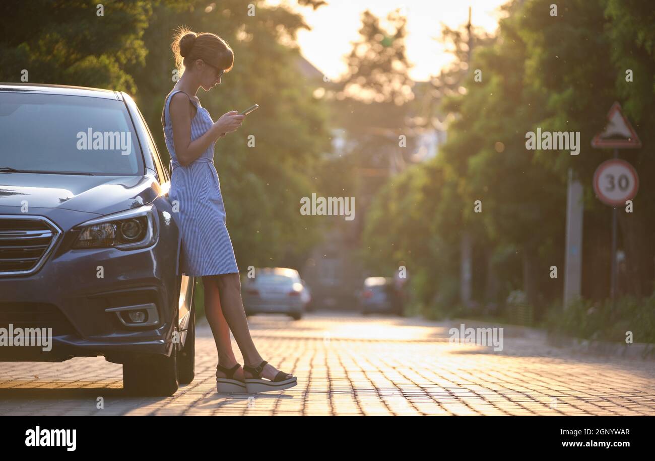Young female driver standing near her vehicle browsing cellphone on a ...