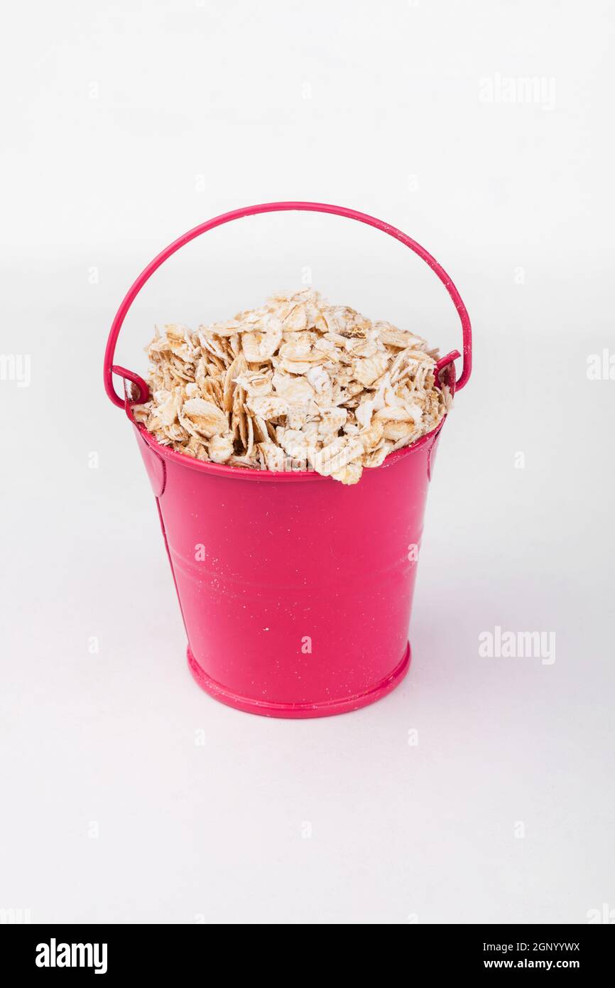 Heap oat-flakes grains in pink bucket on white background. Copy space ...