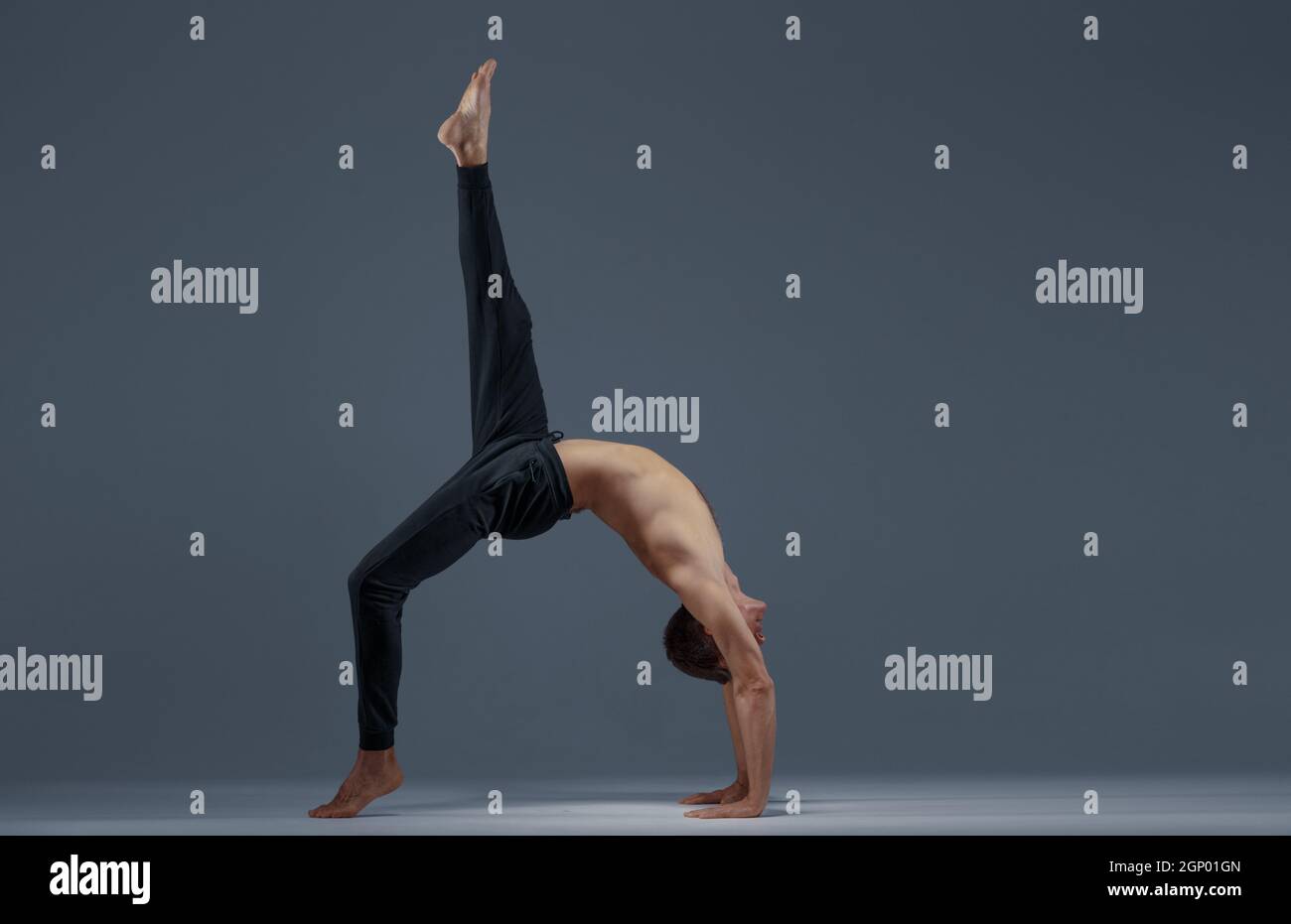 Male yoga doing stretching exercise in studio, grey background. Strong ...