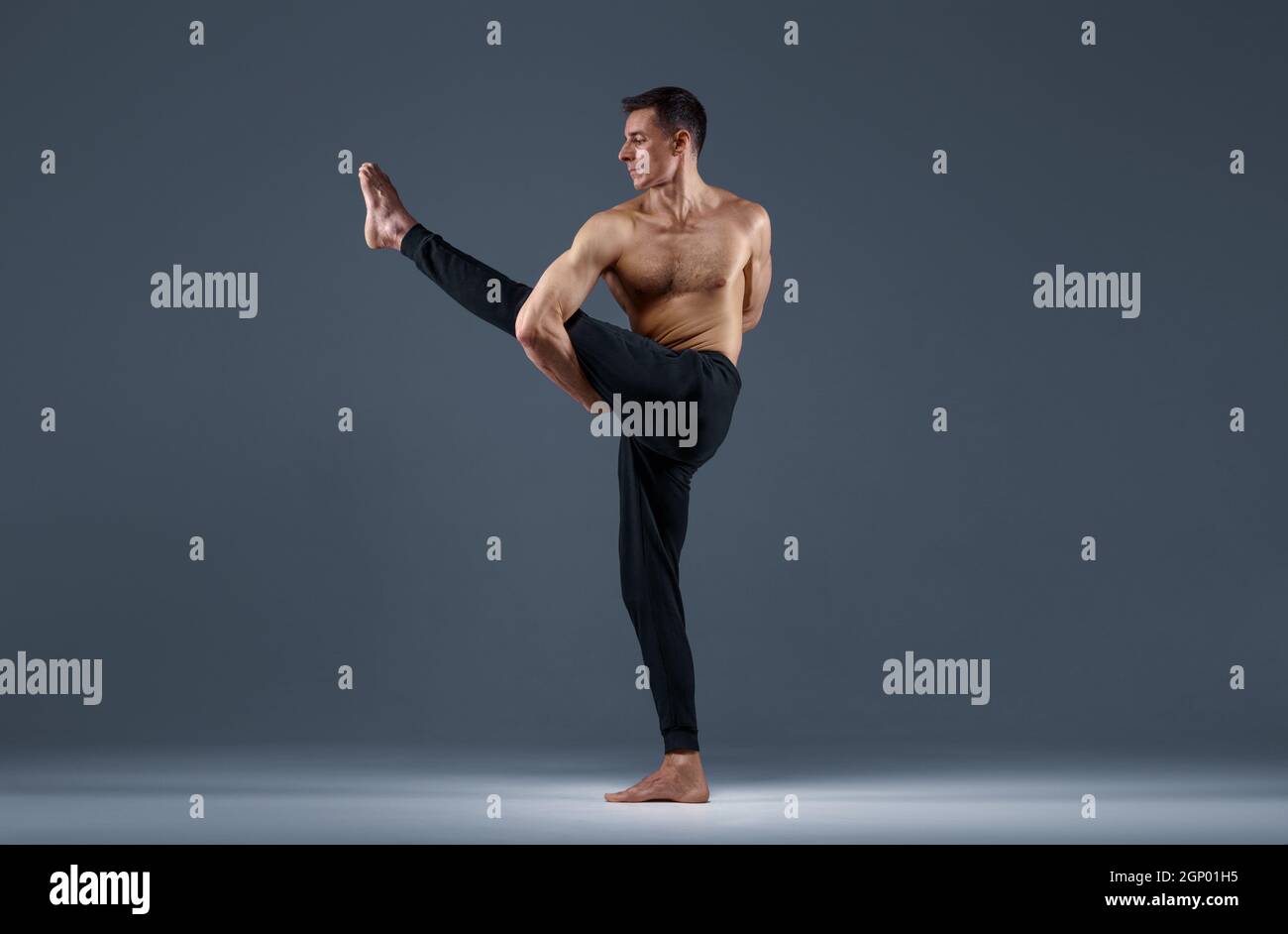 Male yoga doing stretching exercise in studio, grey background. Strong ...