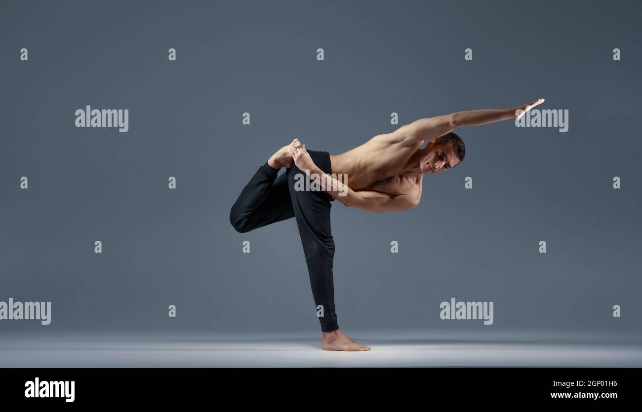 Male yoga keeps balanc in a difficult pose on one leg, grey background ...