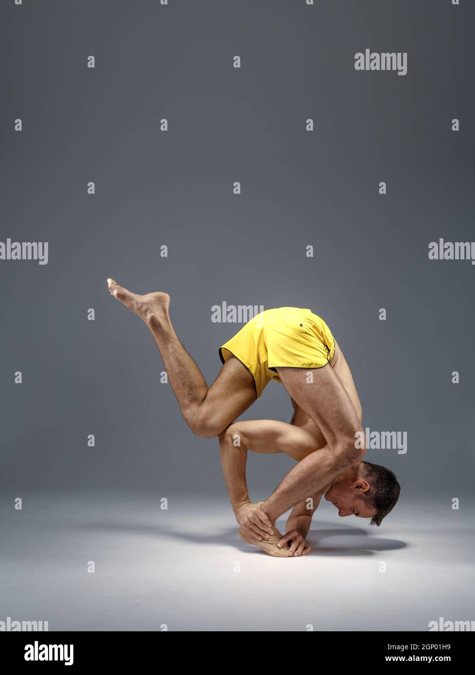 Male yoga in a difficult pose on hands, meditation, grey background ...