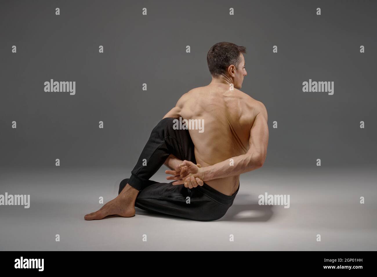 Yoga doing stretching exercise in studio, grey background. Strong man ...