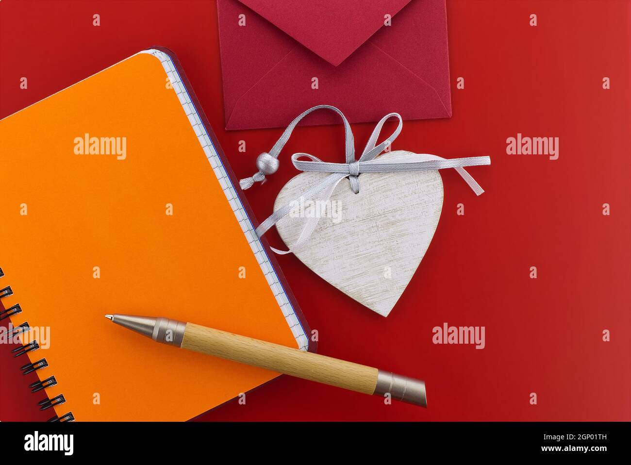 Heart medallion, wire bound notepad, pen and envelope on red background ...