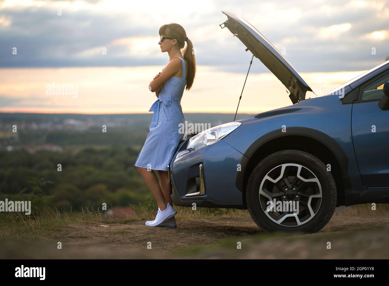 Young female driver standing near a broken car with open up hood ...