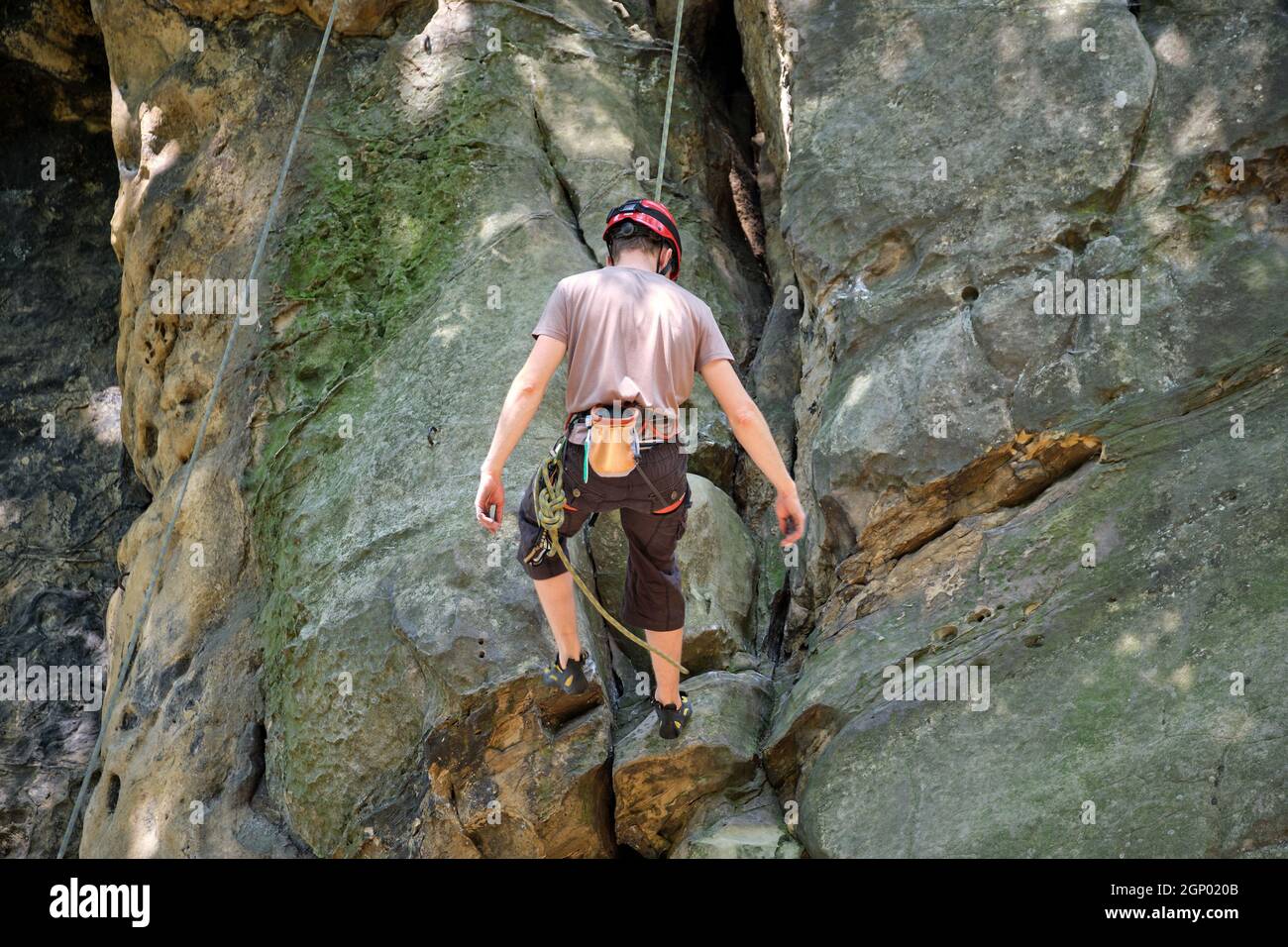 Young man climbing steep wall of rocky mountain. Male climber overcomes ...