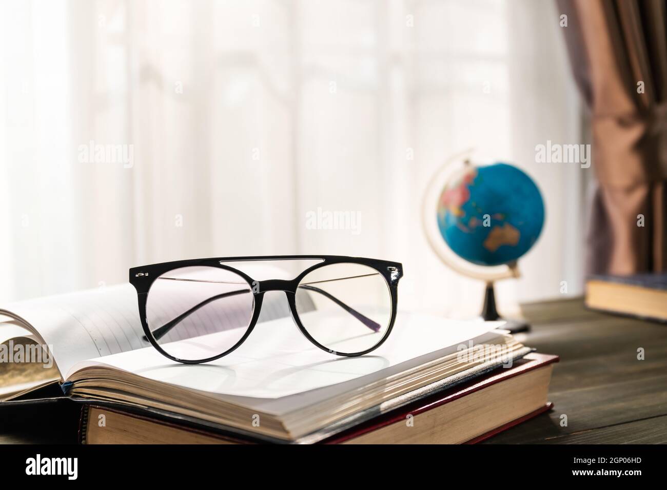 Reading glasses put on open books over wooden table beside the window ...