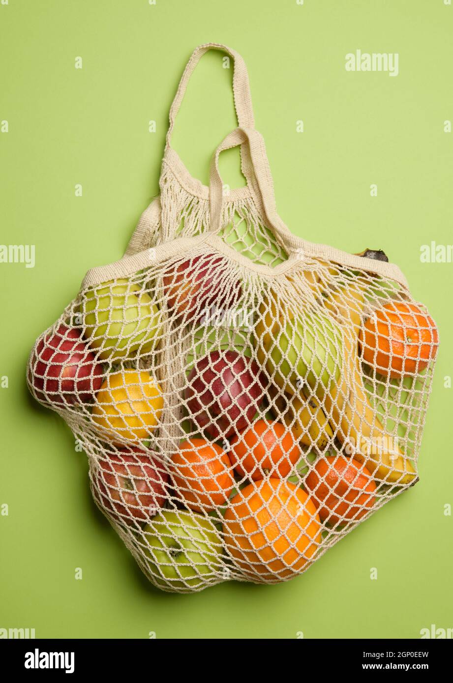 ripe fresh fruits in a textile string bag on a green background, top ...