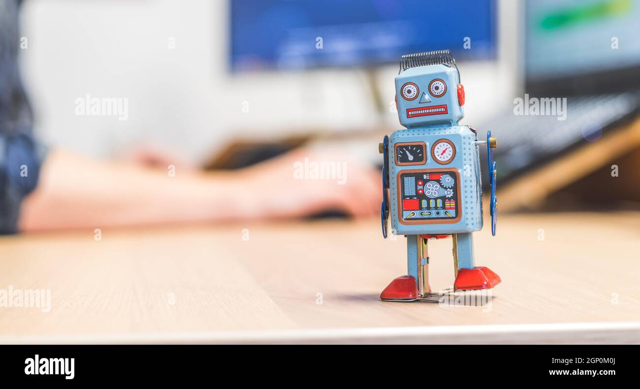 Toy robot on a desktop, man working on the computer in the background ...