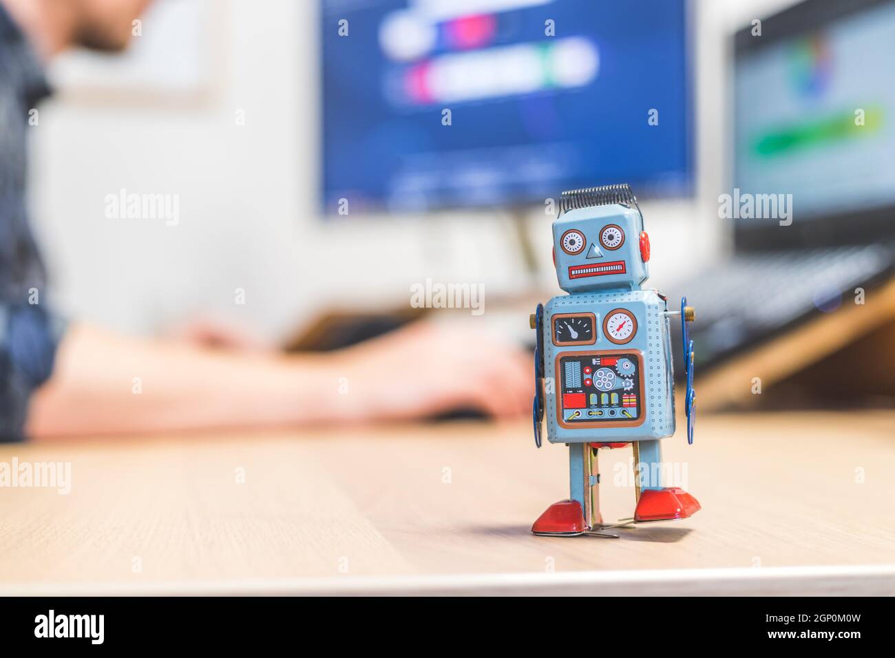 Toy robot on a desktop, man working on the computer in the background ...