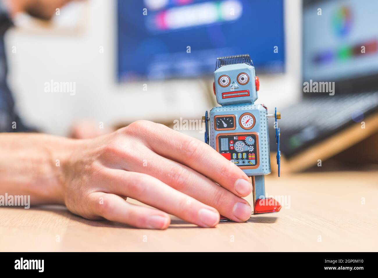Toy robot on a desktop, man working on the computer in the background ...