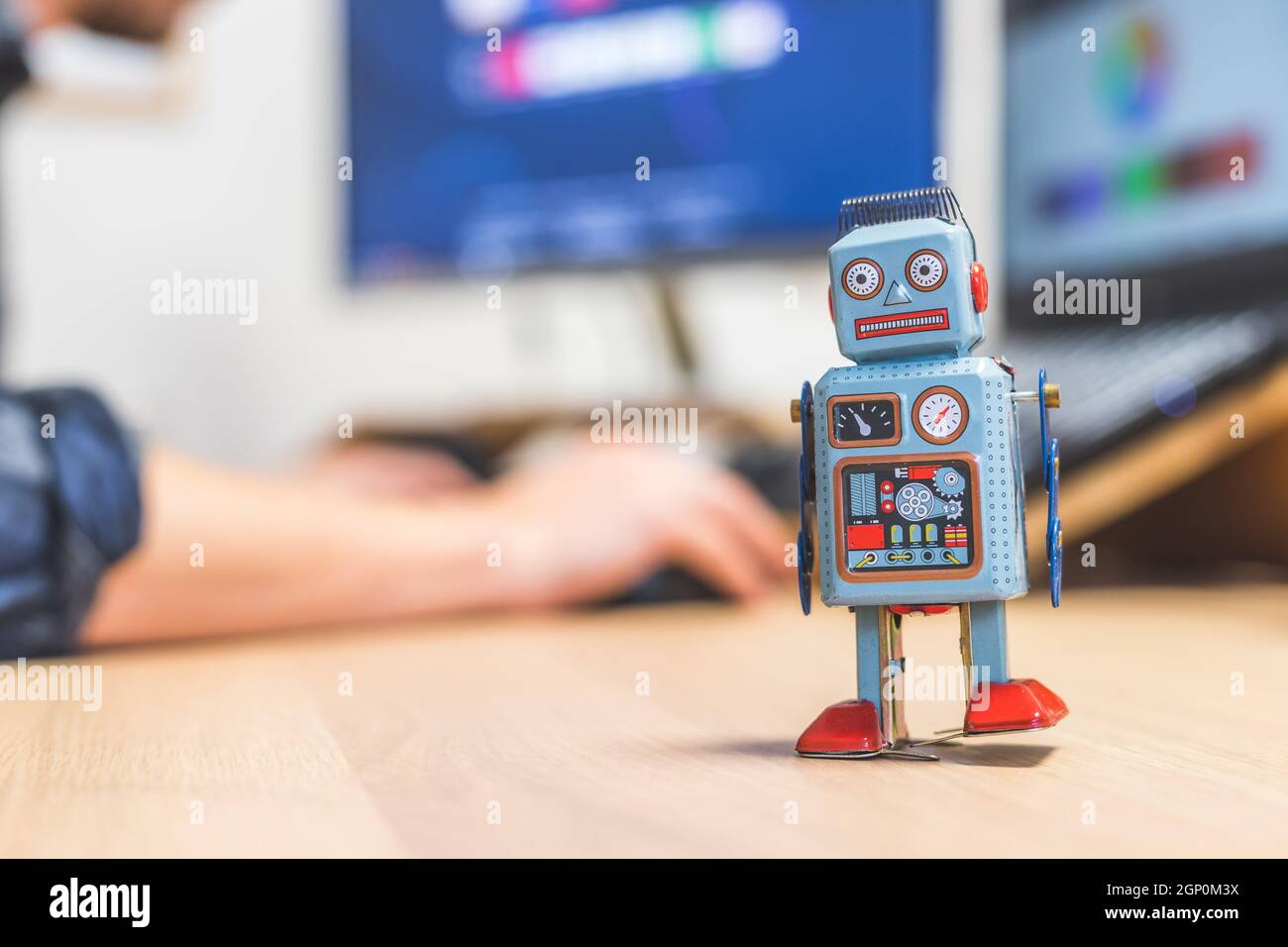 Toy robot on a desktop, man working on the computer in the background ...