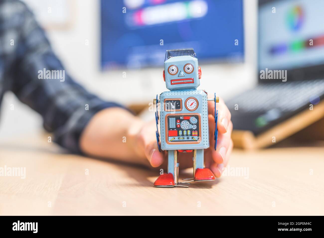 Toy robot on a desktop, man working on the computer in the background ...