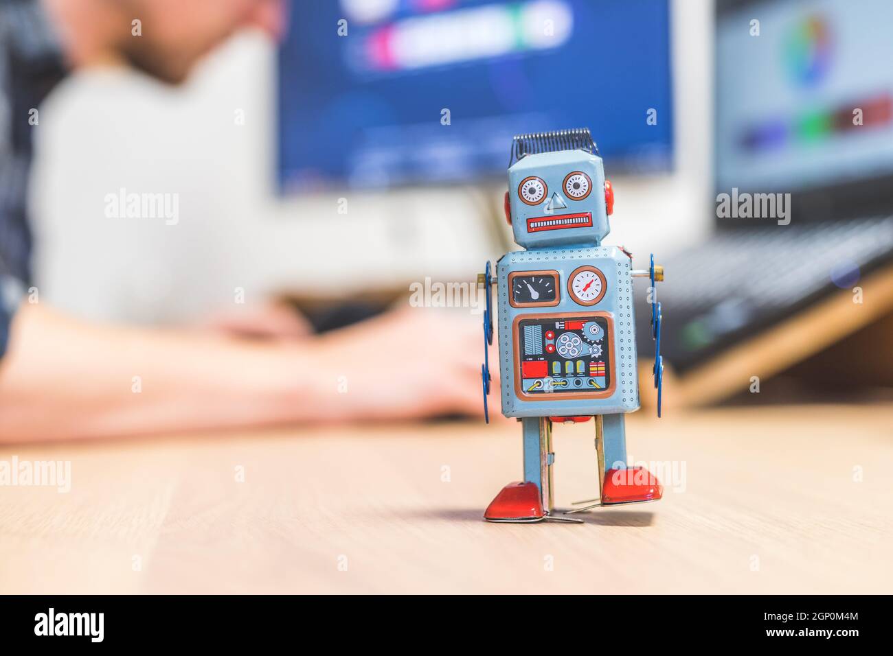 Toy robot on a desktop, man working on the computer in the background ...