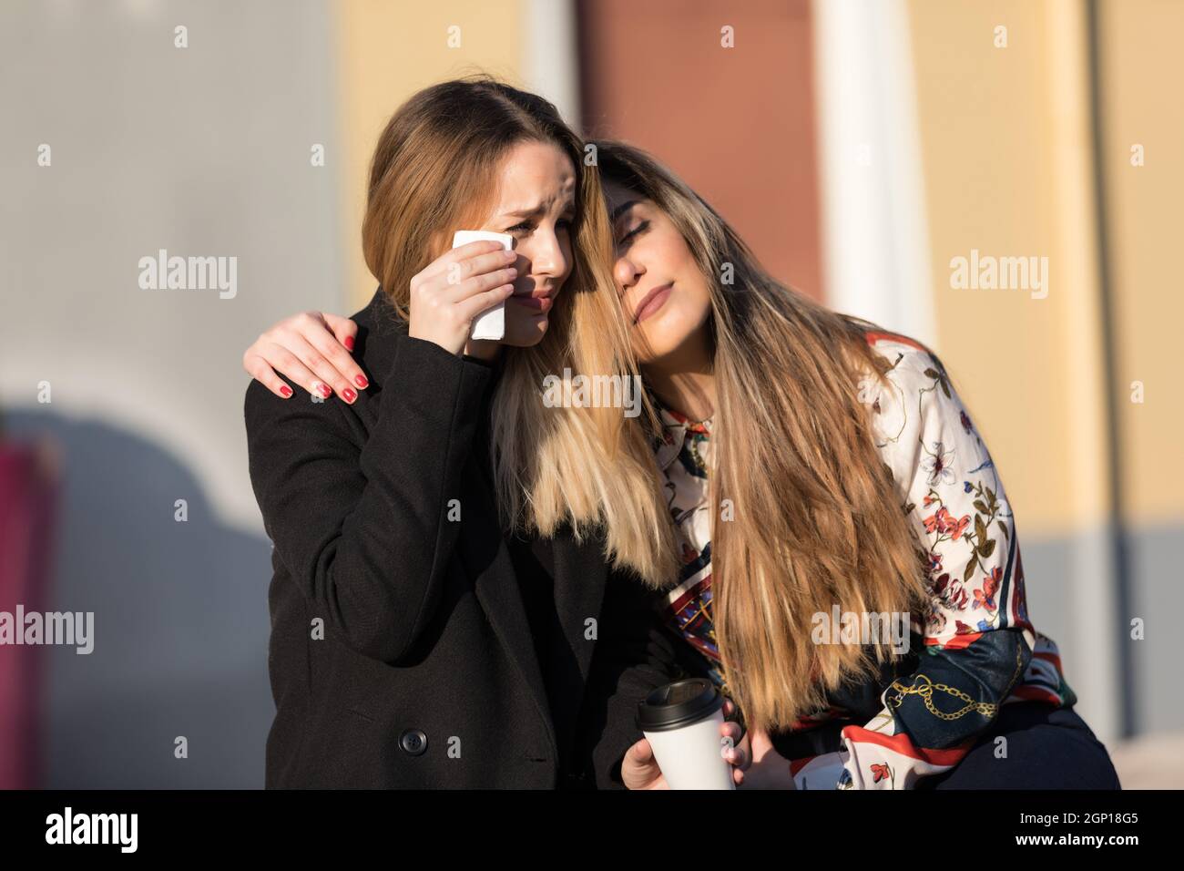 Young woman cheering up crying female friend at the street with ...