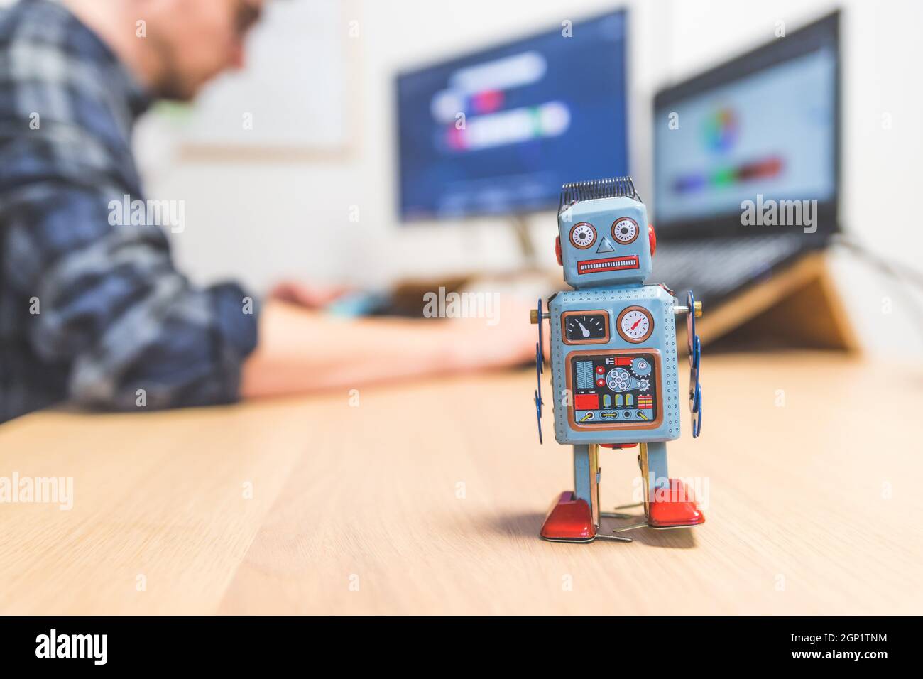Toy robot on a desktop, man working on the computer in the background ...