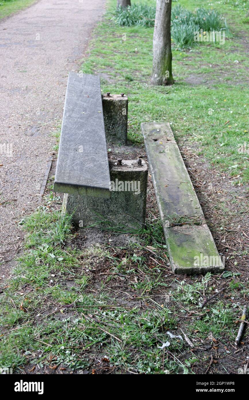 Damaged park bench seat on concrete legs with a plank on the ground ...