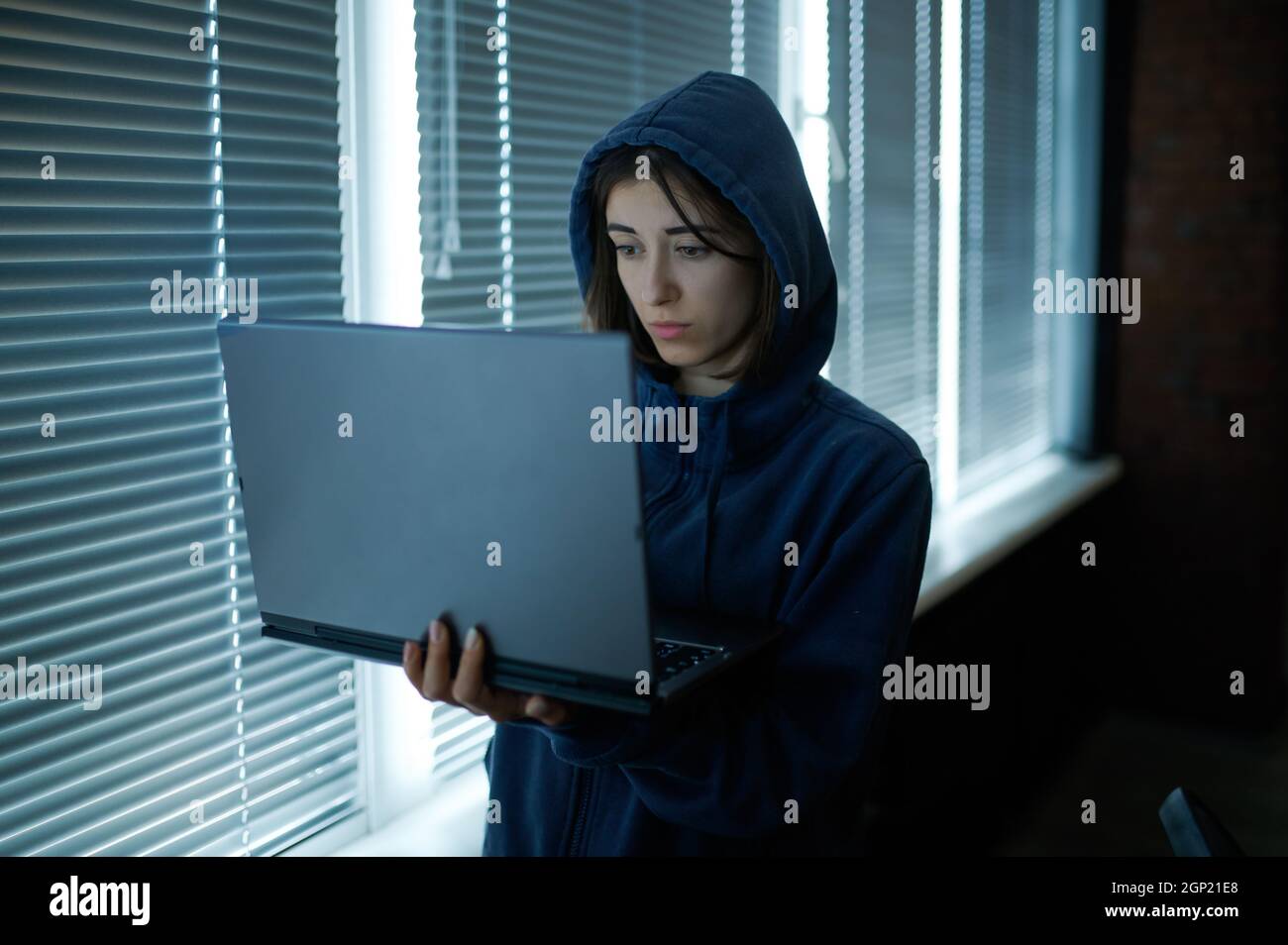 Female internet hacker in hood works on laptop in dark office. Illegal ...