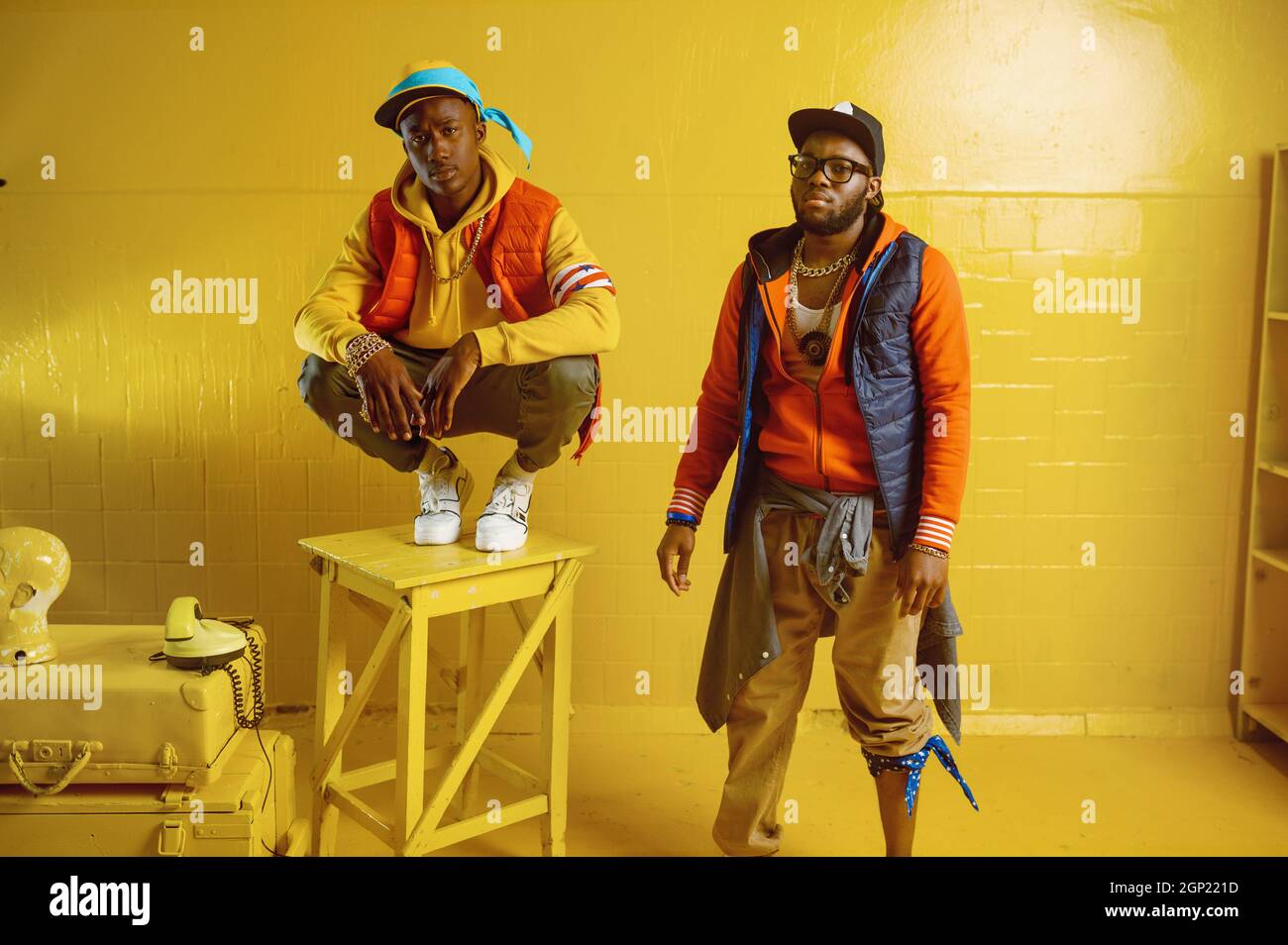 Two stylish rappers with gold jewelry in cool studio, yellow background ...
