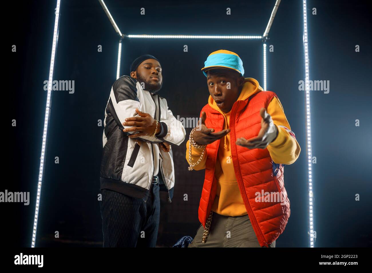Two stylish rappers poses in glowing cube, studio with dark background ...