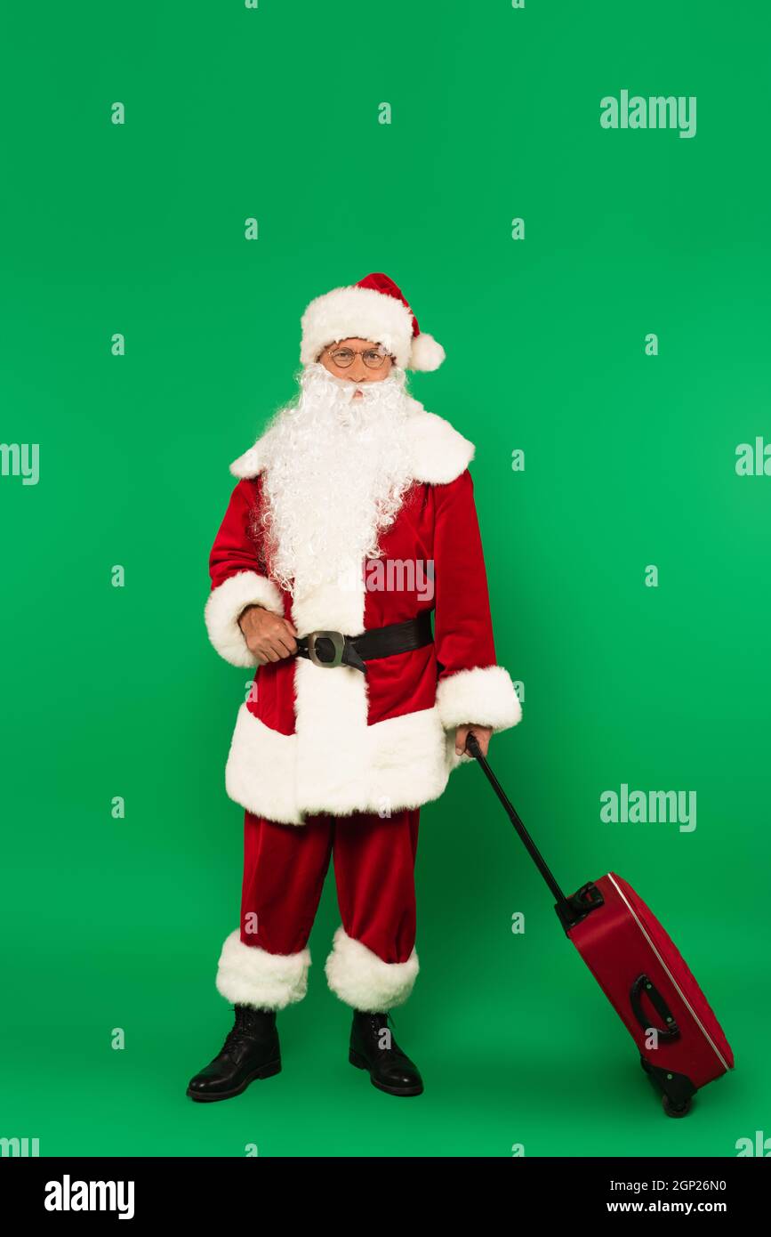 Santa claus in costume holding suitcase on green background Stock Photo ...