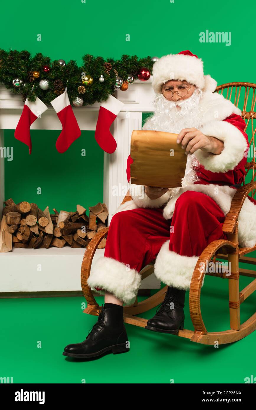 Santa claus with paper sitting on rocking chair near fireplace with fir ...