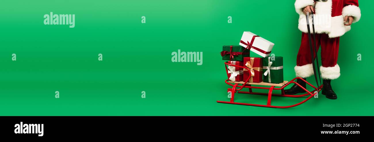 Cropped view of santa claus in costume standing near presents on sleigh ...