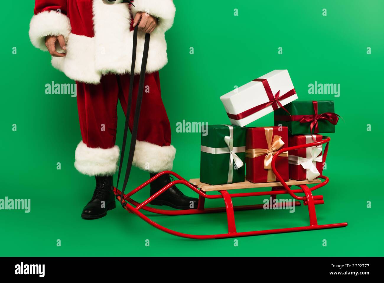 Cropped view of santa claus standing near gifts on sleigh on green ...