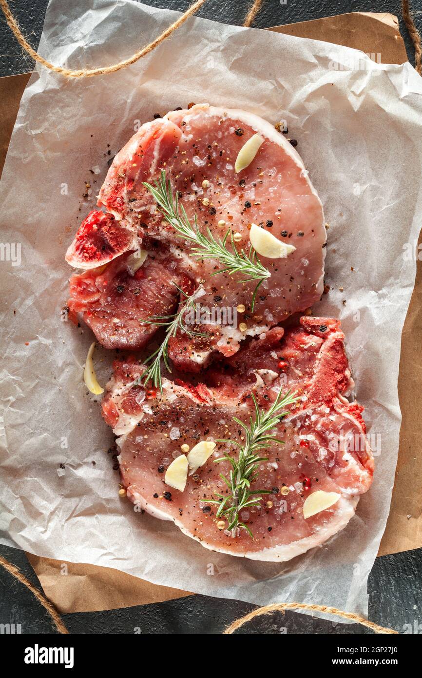 Two raw pork steaks grey stone background with rosemary and spices. Top ...
