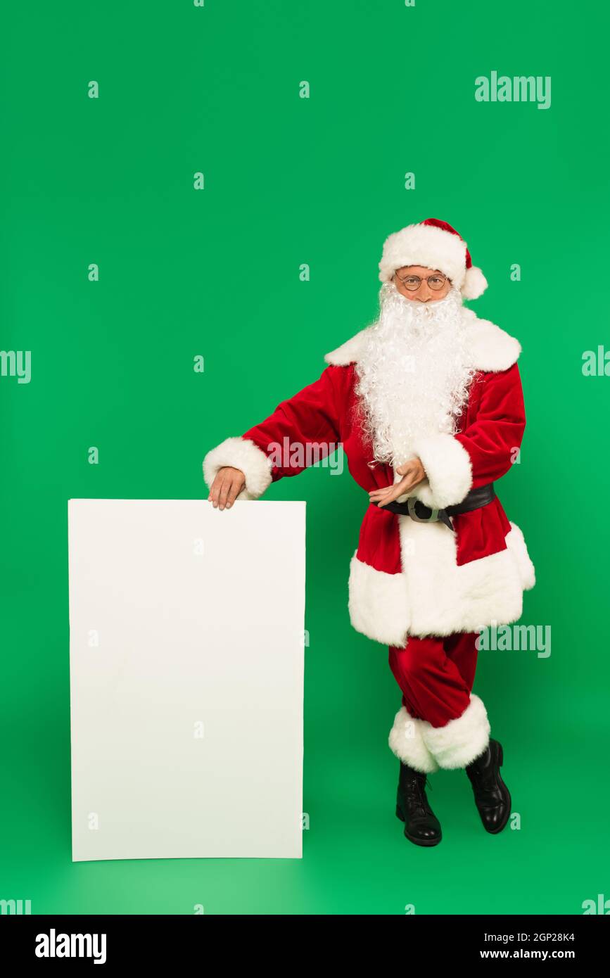 Santa claus pointing at white placard on green background Stock Photo ...