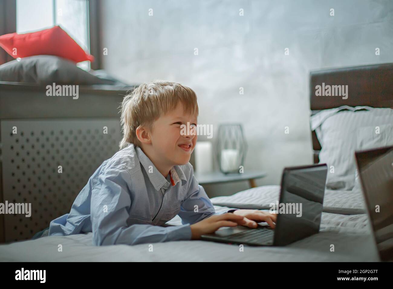 schoolboy boy kneels in bedroom and plays games on laptop. happy child ...