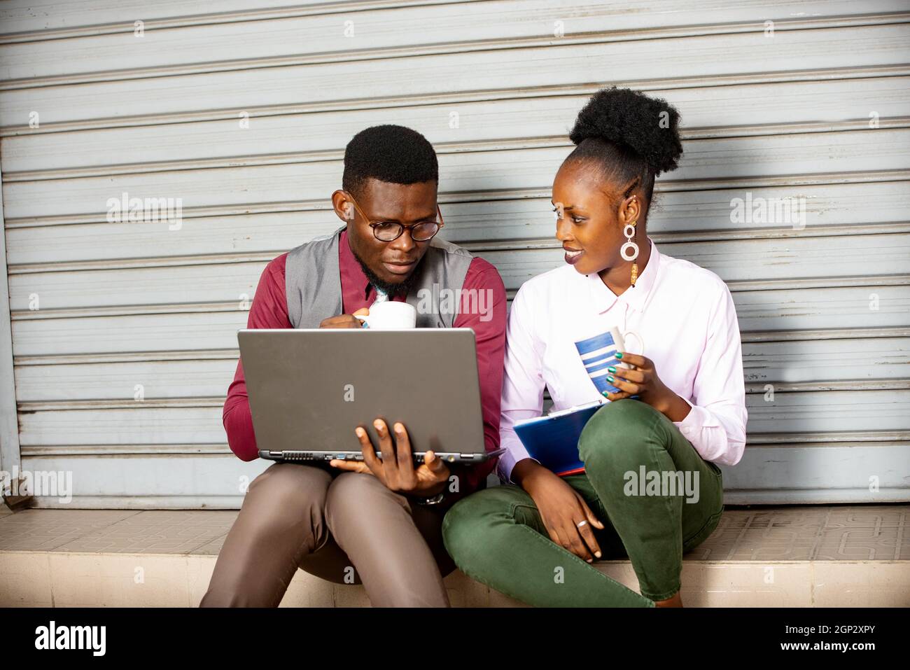 young business people sitting outside on steps working using a laptop ...