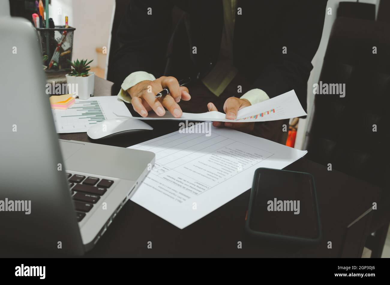 Business men look at business documents and hold pens with computer ...