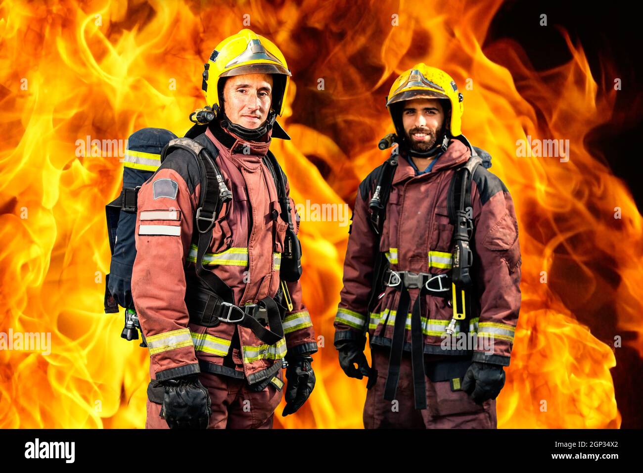 Conceptual portrait of two firemen standing against burning fire ...
