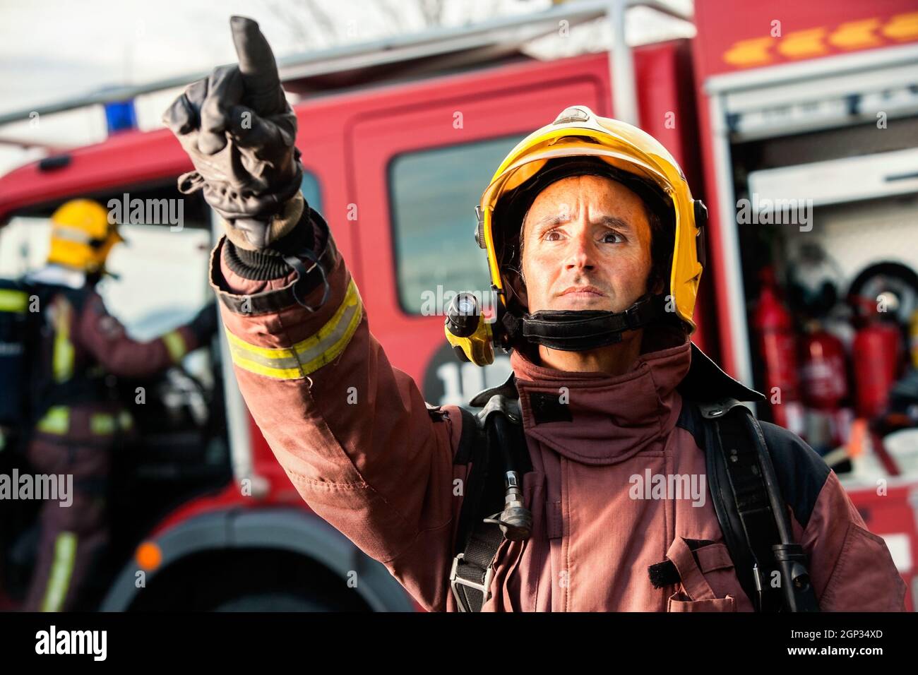 Anxious fireman with fire truck in background pointing at danger ...