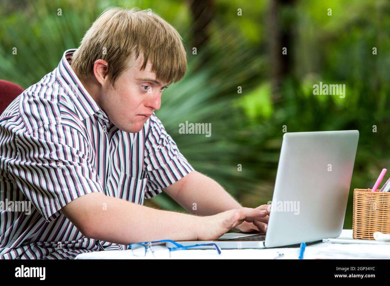 Portrait of concentrated young man with down syndrome working on laptop ...