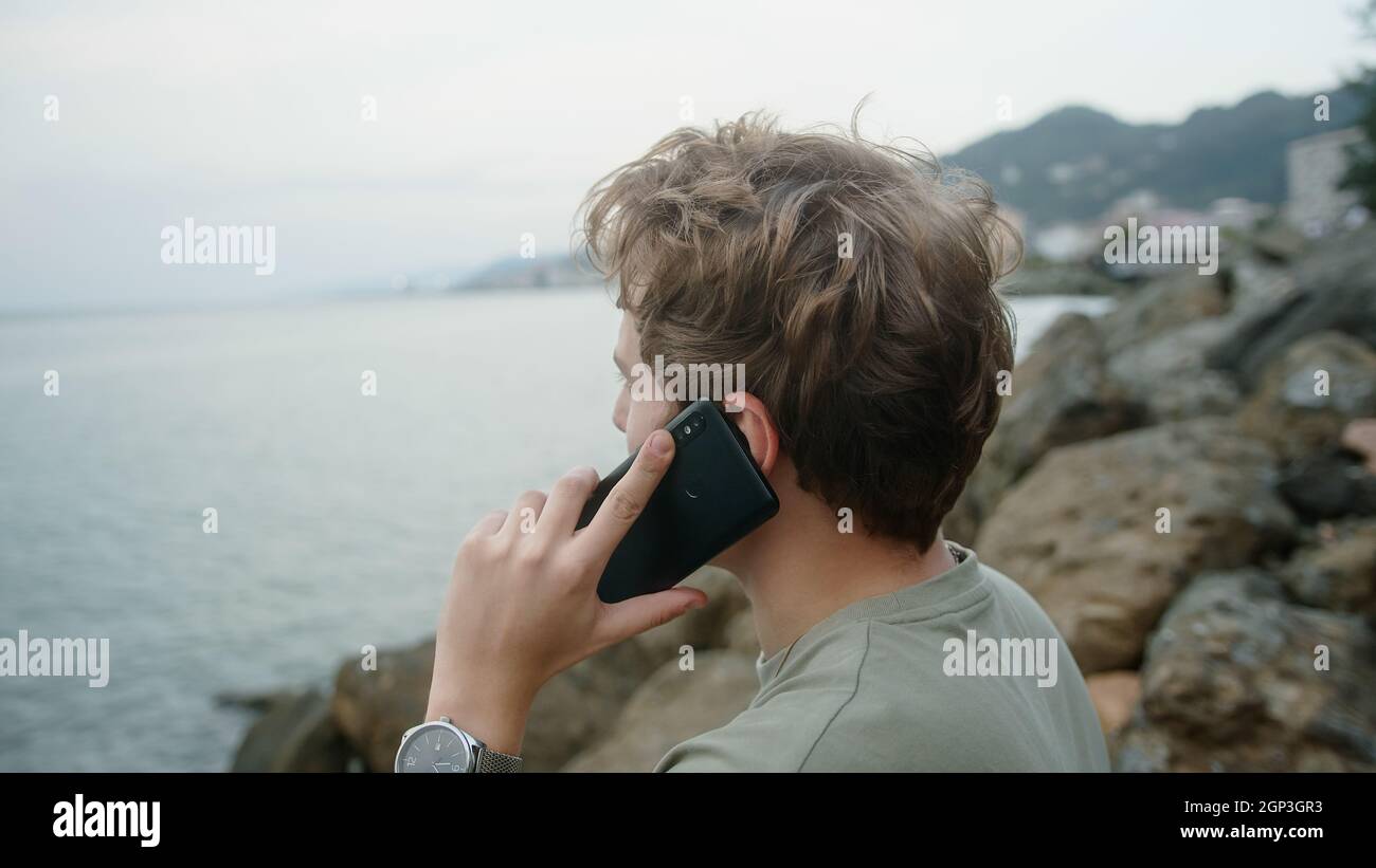 Handsome blond boy making phone call with smartphone by the sea Stock ...