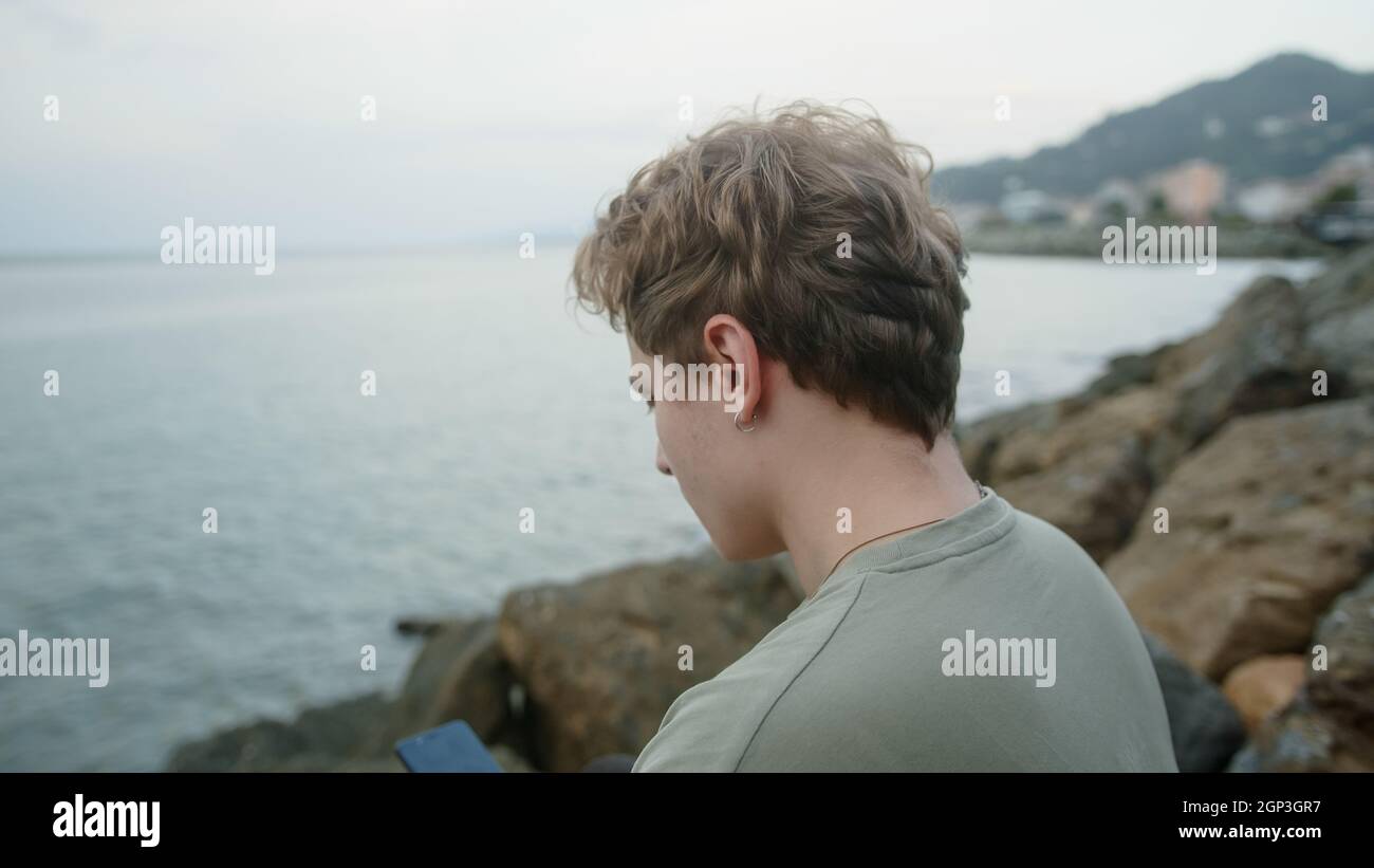 Handsome blond boy making phone call with smartphone by the sea Stock ...