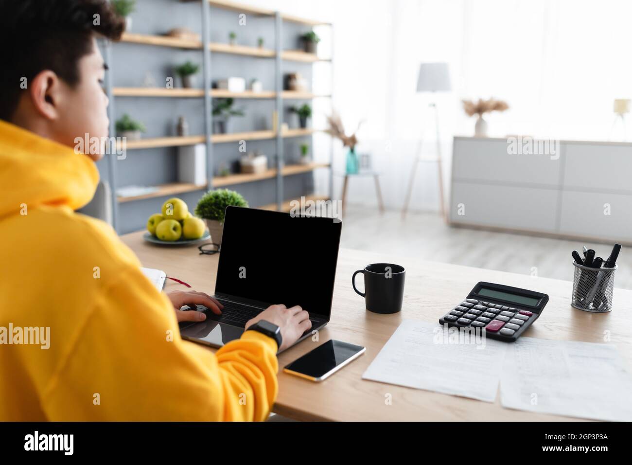 Over the shoulder view of busy asian guy working on laptop in home ...
