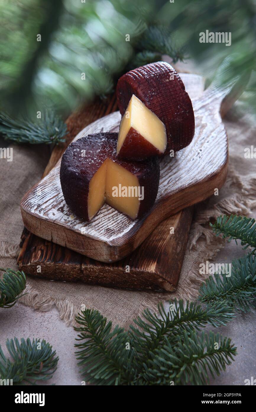 Hard wine cheese on a wooden board. Spruce branches. Vertical photo on ...