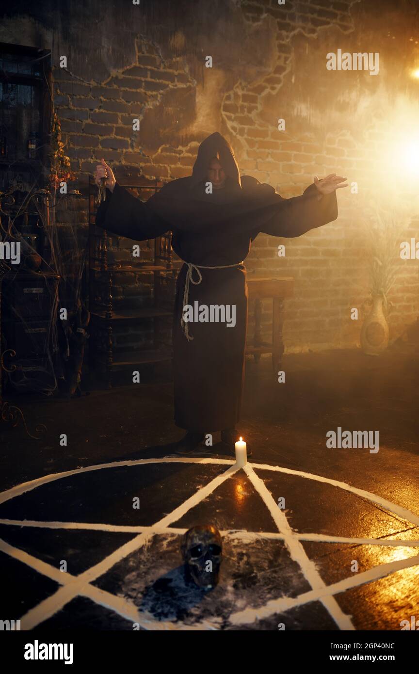 Male exorcist in black hood reads a spell near the magic circle ...