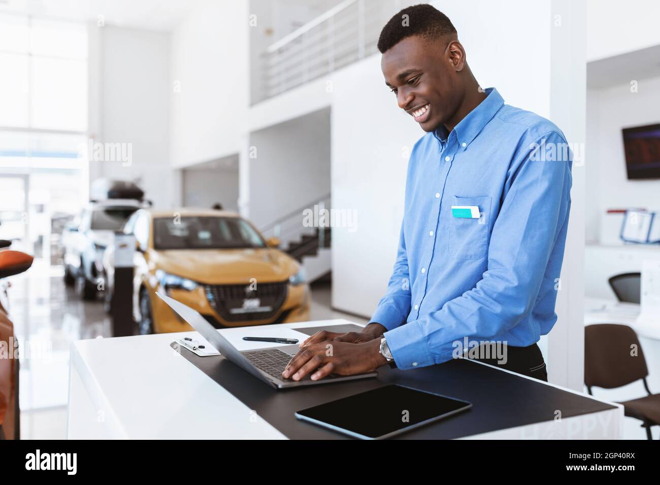 Positive black car salesman using laptop computer at work desk in auto ...