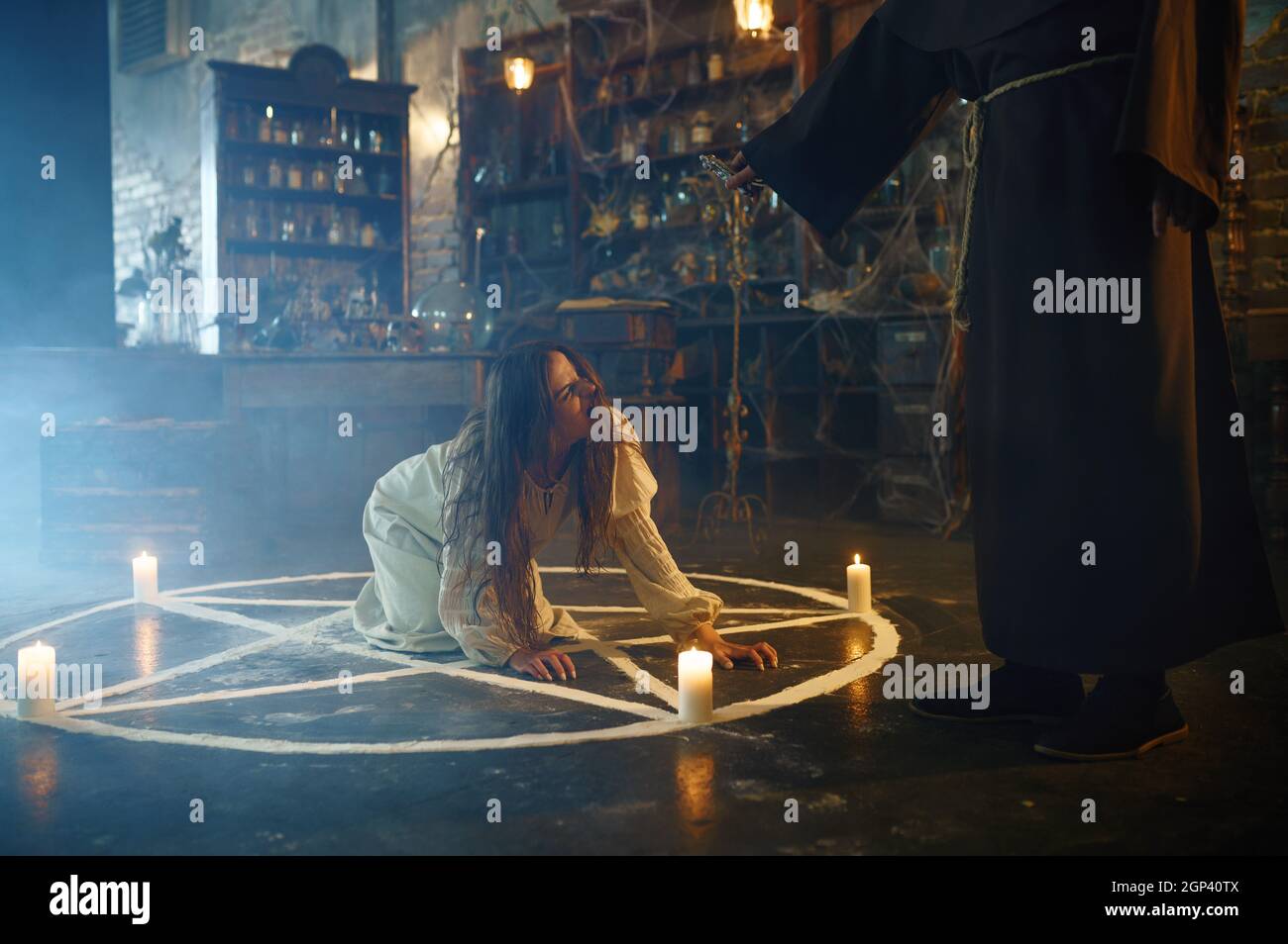 Male exorcist in black hood casting out devil from a woman. Exorcism ...