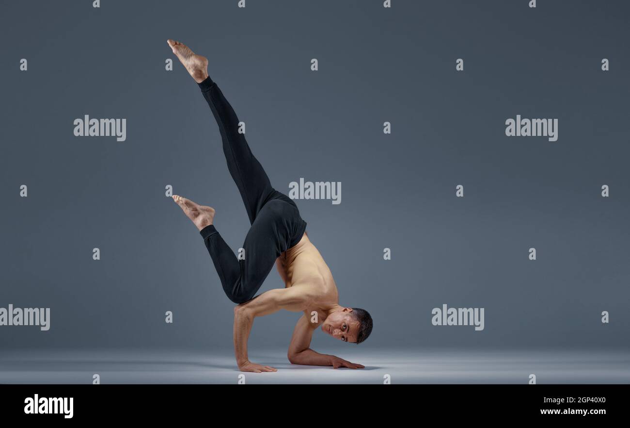 Male yoga keeps balanc in a difficult pose on hands, grey background ...