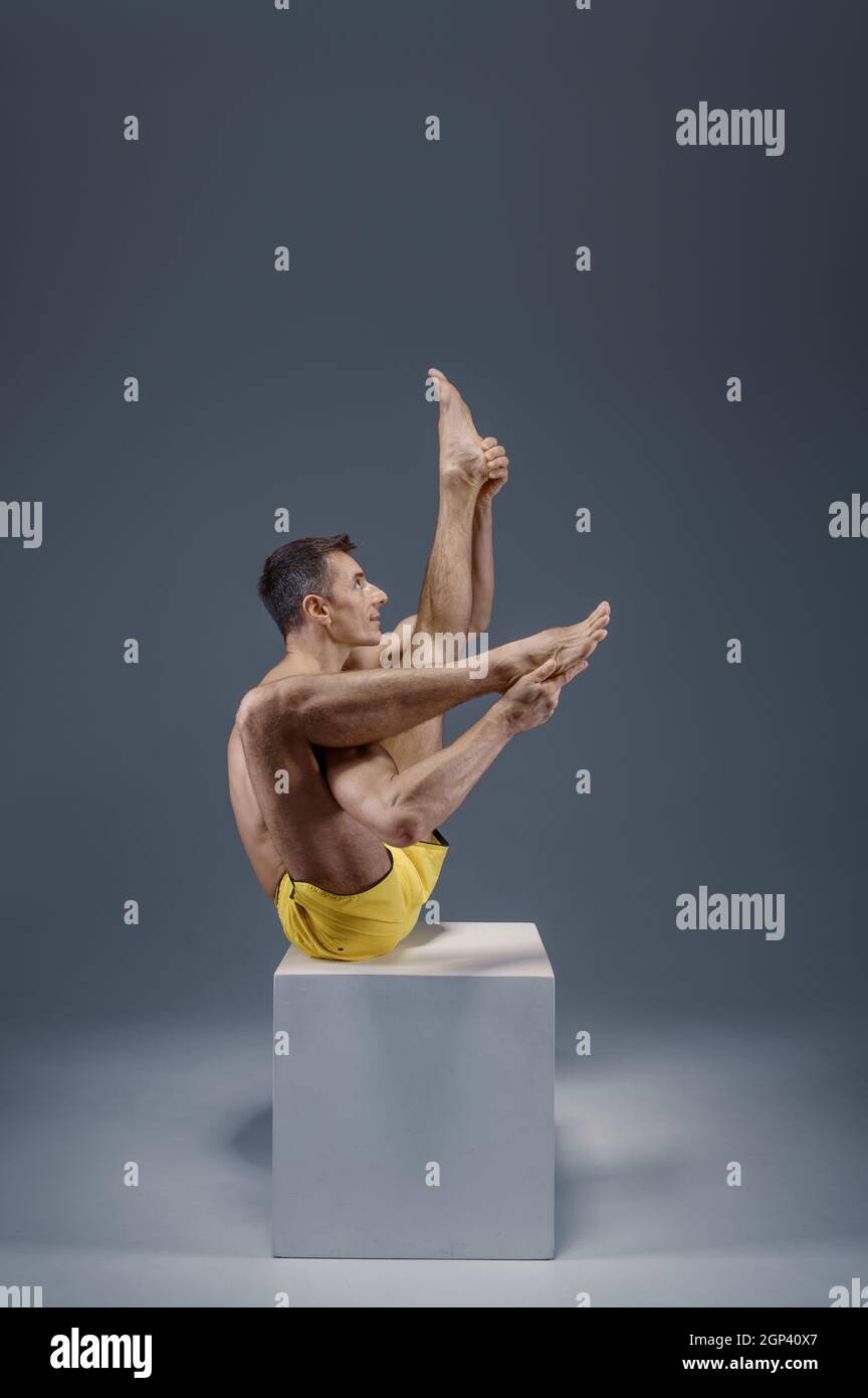 Male yoga sitting on the pedestal in studio, meditation position, grey ...